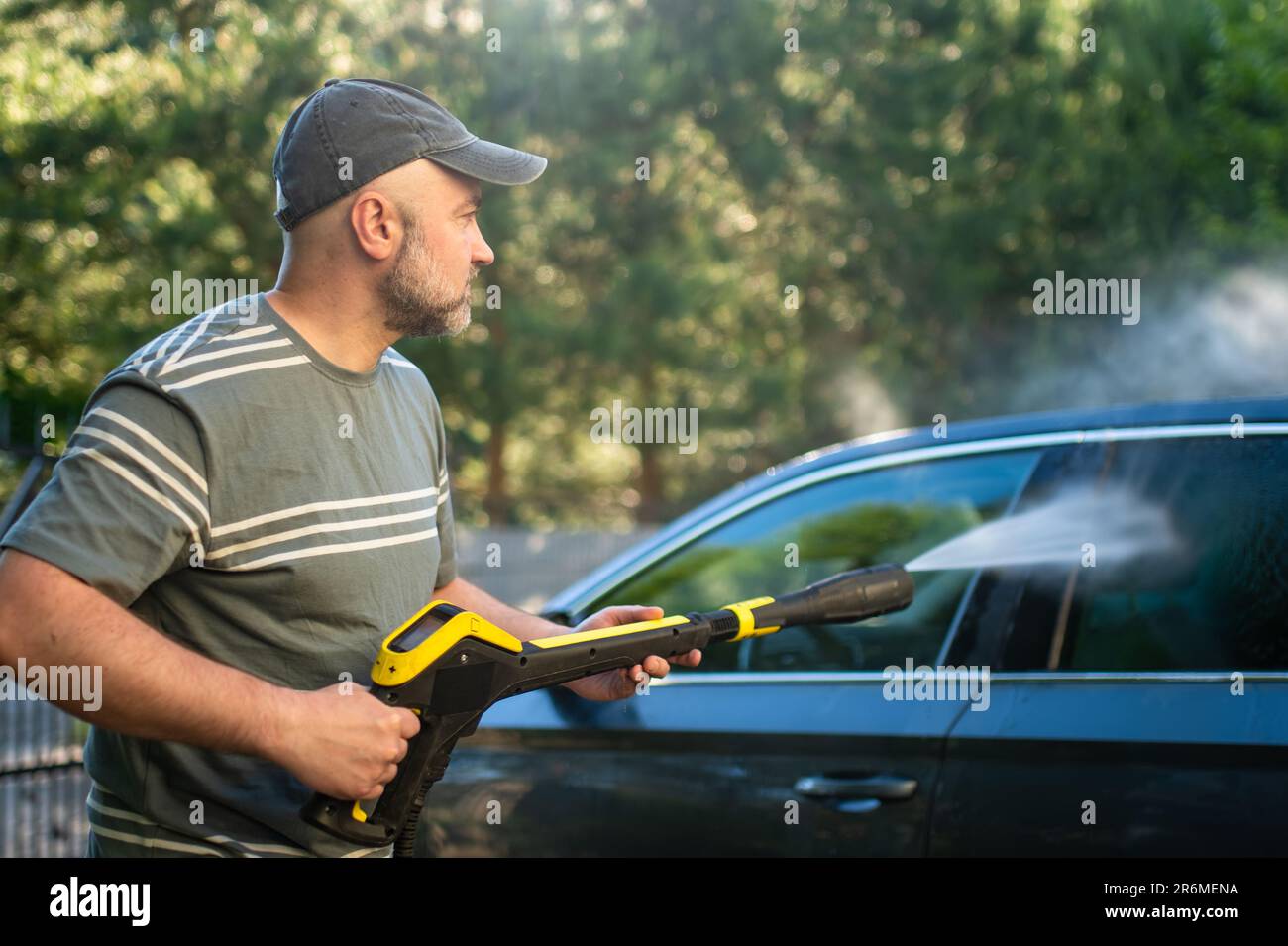Ein junger Mann, der sein Auto mit einer Wasserpistole wäscht ...