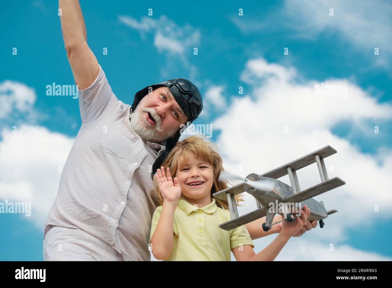 Lustige Großvater und Sohn spielen mit Holzflugzeug vor Sommerhimmel ...