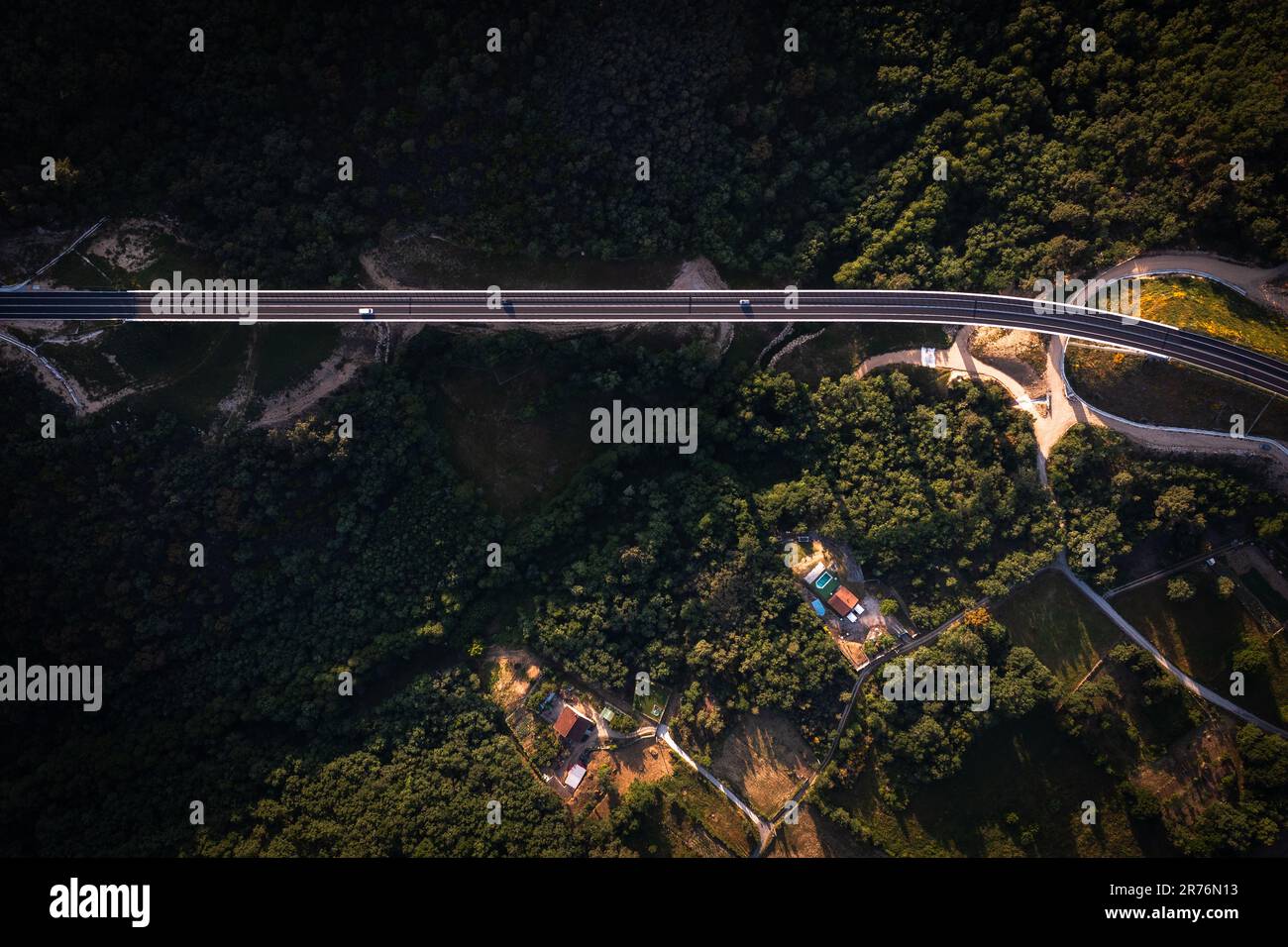 Draufsicht über die moderne Hängebrücke über das dunkelgrüne Tal mit Gebäuden und Fahrzeugen ...