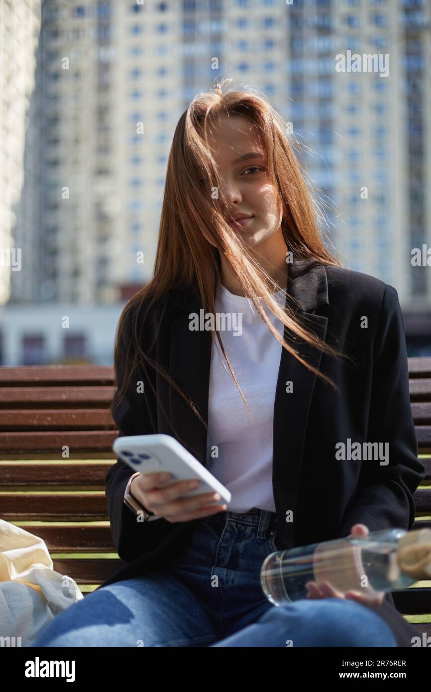 Wunderschöne junge Frau, die auf einer Bank sitzt, mit einem Smartphone ...