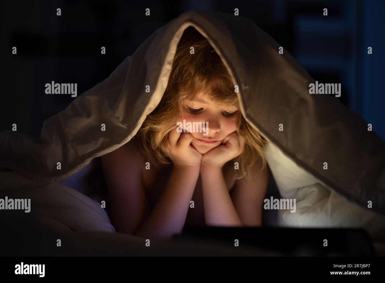 Ein Kind, das nachts auf einem Tablet im Bett spielt. Kinder mit ...