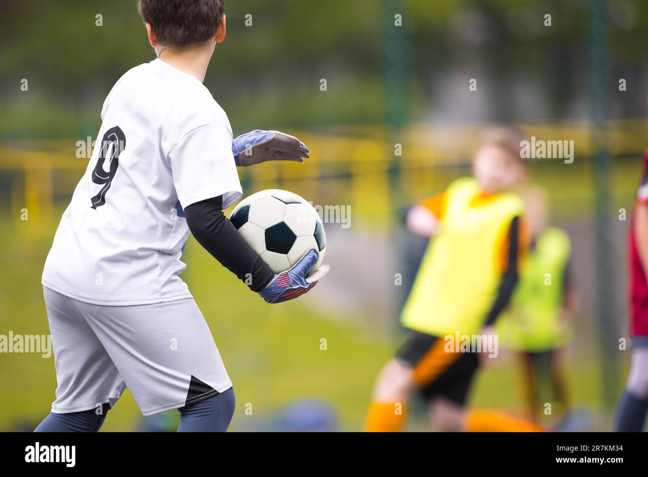 Kleiner Junge als Fußballtreffer, der den Ball in einer Hand hält und ...