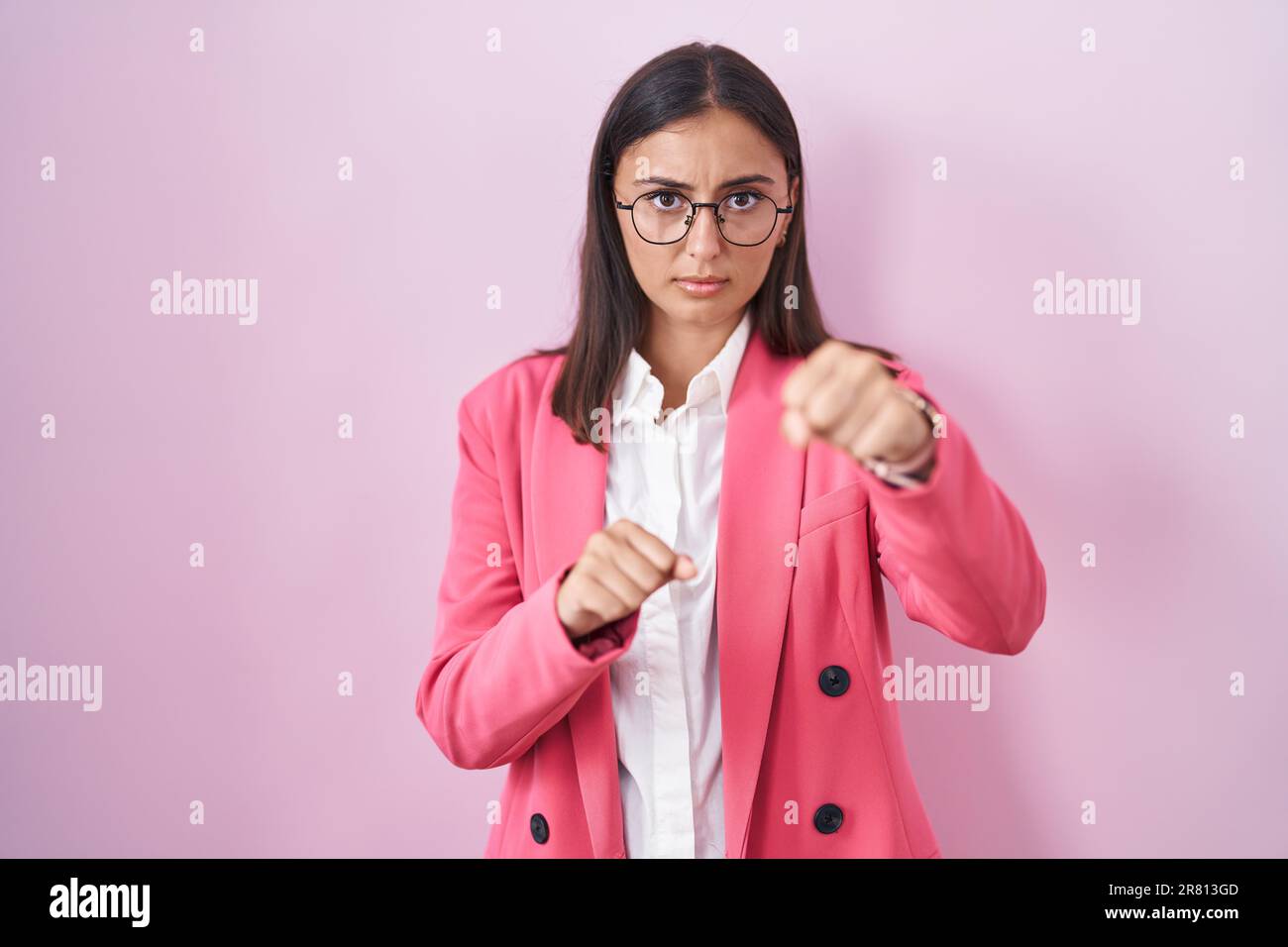 Junge hispanische Frau in Geschäftskleidung und Brille, die Faust schlägt, um zu kämpfen ...