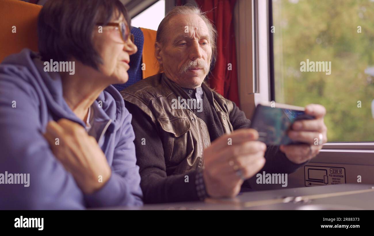 Ältere Paare reisen mit dem Zug, die Seniorin hält ein Handy in der ...