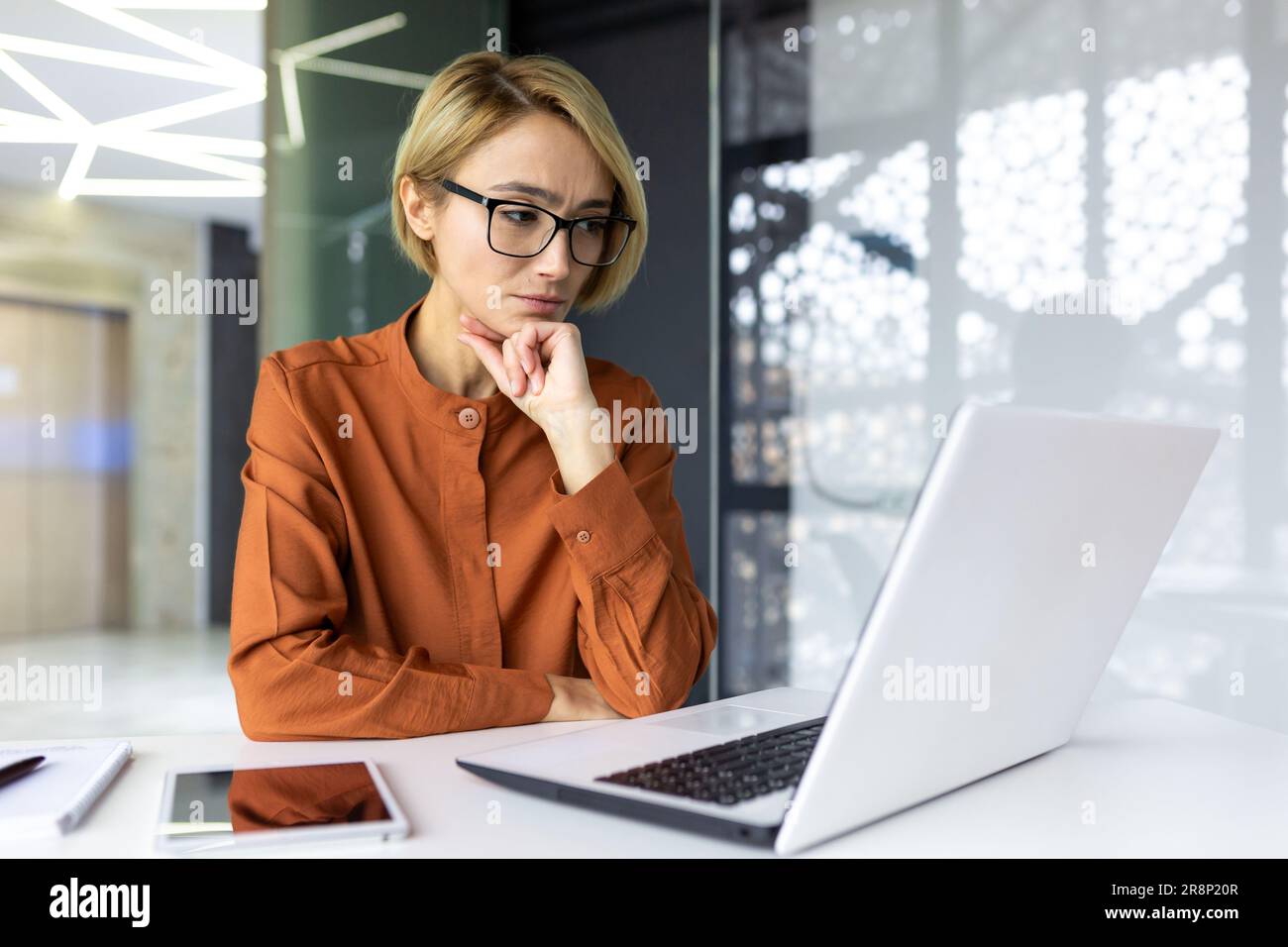Ernsthaft denkende Frau, die im Büro mit einem Notebook arbeitet ...