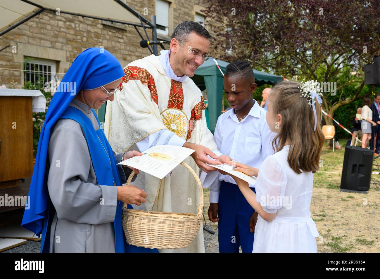 Ein Priester, der jedem Kind, das die erste Heilige Kommunion erhalten hat, eine Medaille und ...