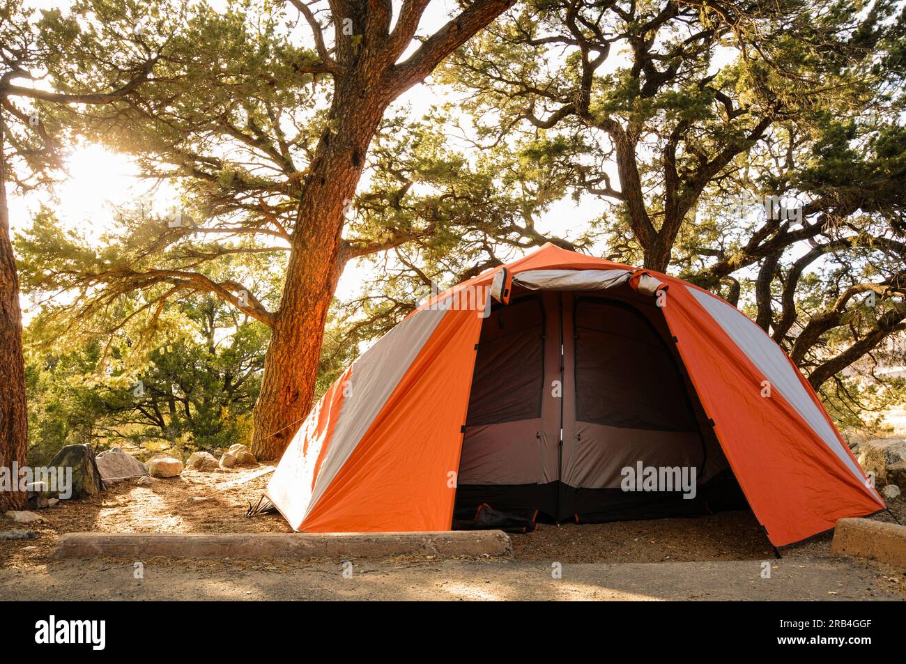 Ein großes orangefarbenes Zelt mit Abendsonne, die durch die Bäume auf dem Campingplatz der ...