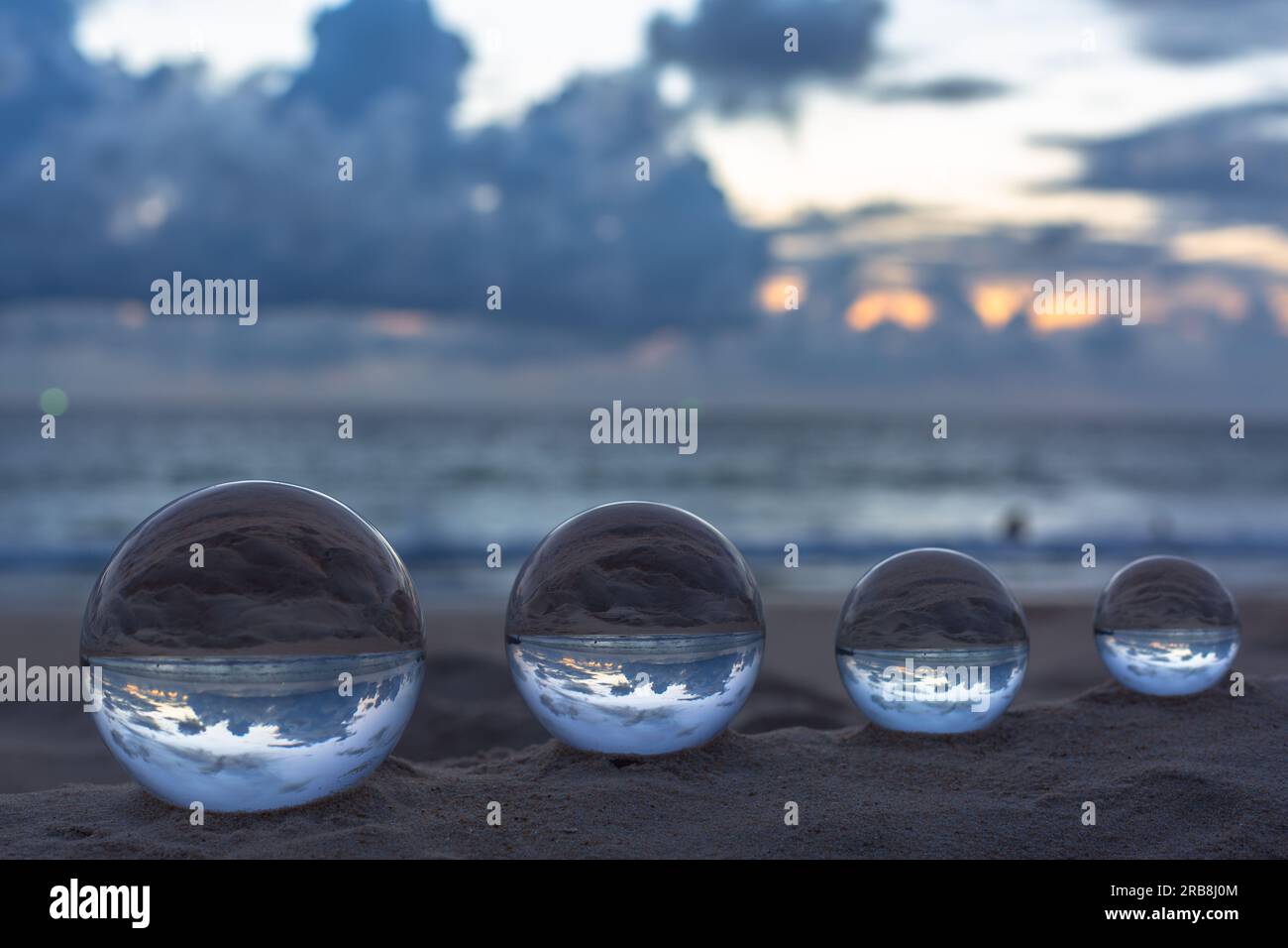 Die 4 Glaskugeln sind bei Sonnenaufgang von groß bis klein am Strand ...