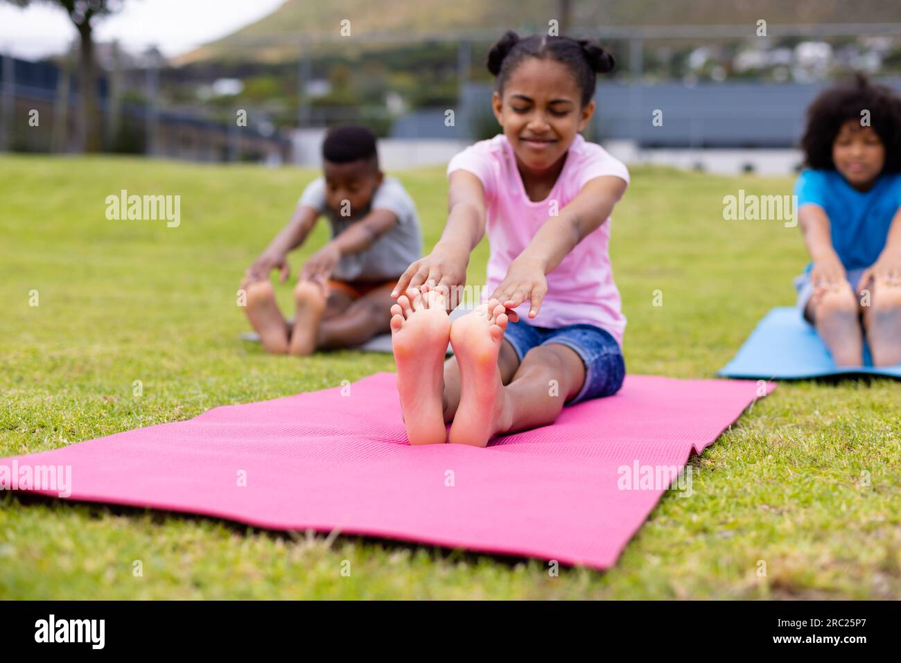 Glückliche afroamerikanische Schulkinder, die Yoga machen und sich in der Schule auf dem ...