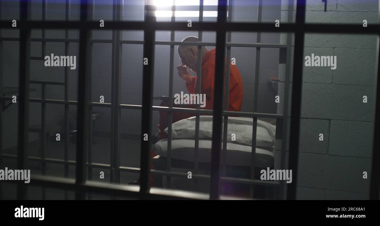 Ältere Gefangene in orangefarbener Uniform sitzen in Gefängniszellen und essen Essen. Der ...