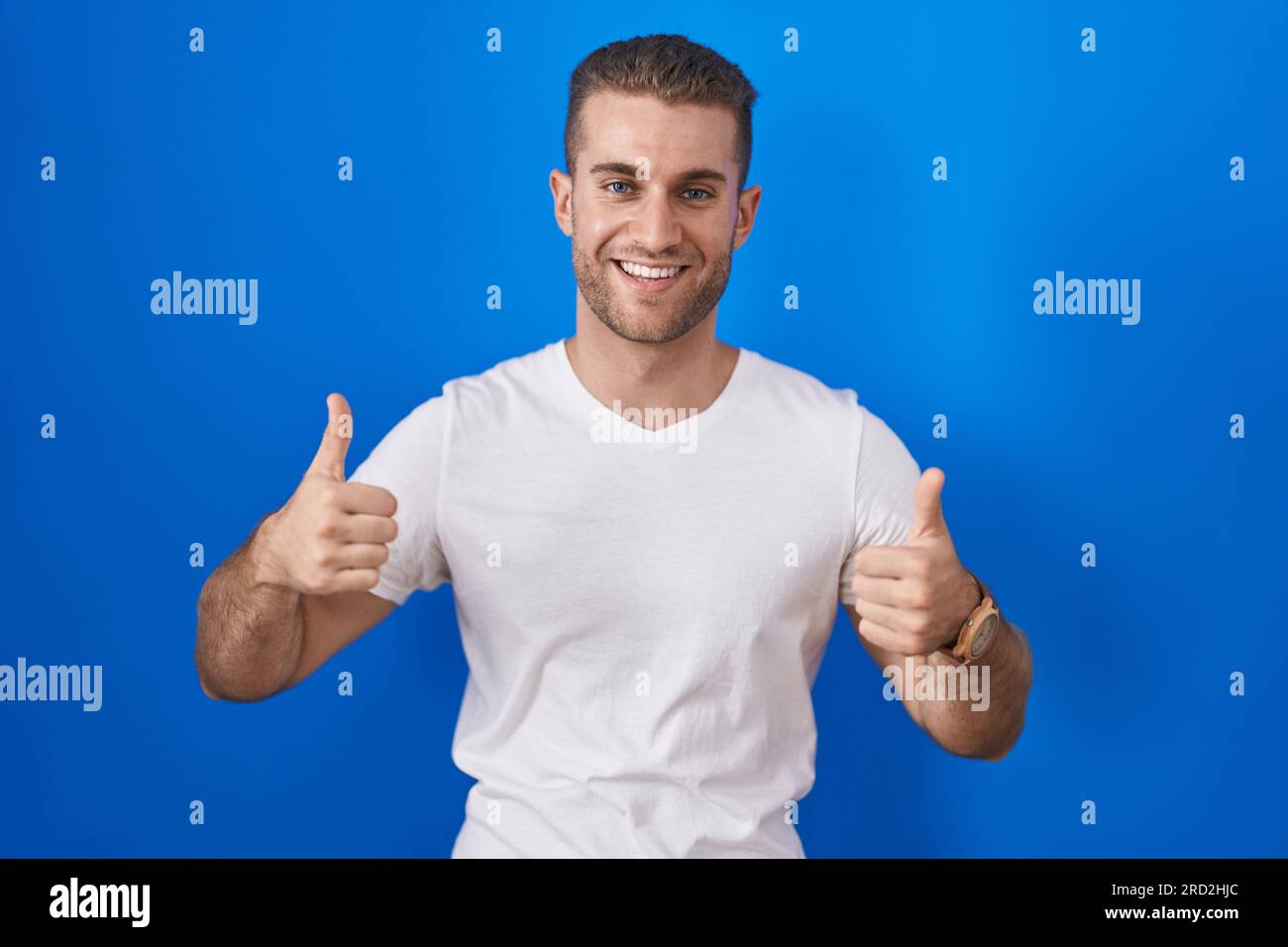 Junger weißer Mann, der über einem blauen Hintergrund steht und mit der ... Junger weißer Mann, der über einem blauen Hintergrund steht und mit der ...
