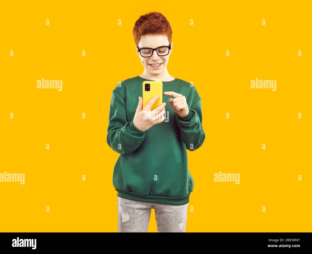 Ein hübscher lächelnder Junge mit Brille und rotem Haar, der auf seinem Mobiltelefon durch die ...