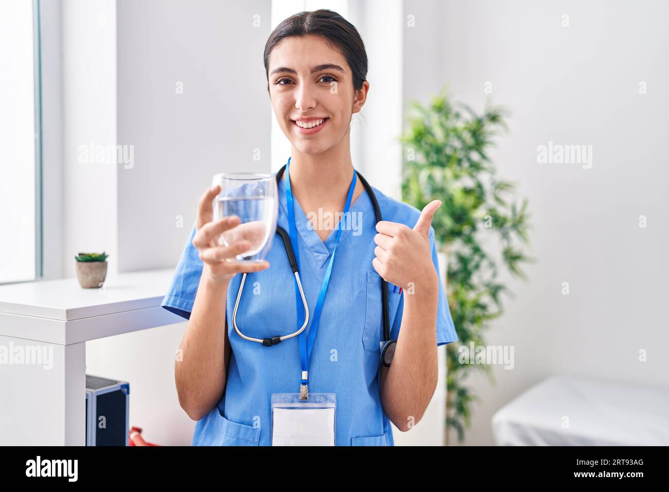 Junge schöne Frau in Arztuniform und Stethoskop Trinkwasser lächelnd ... Junge schöne Frau in Arztuniform und Stethoskop Trinkwasser lächelnd ...