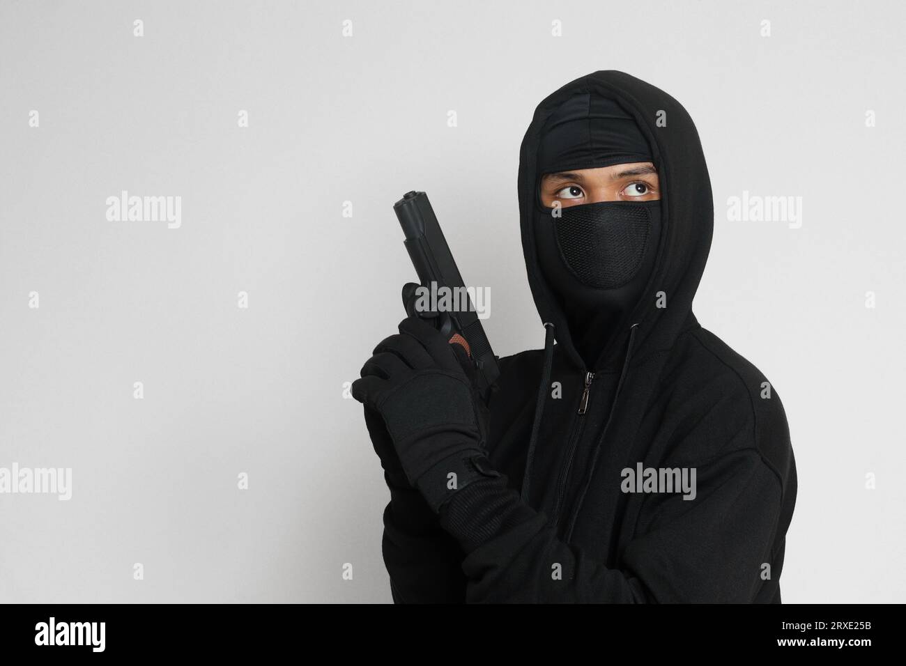 Mysteriöser Mann mit schwarzem Hoodie und Maske, der eine Pistole hält ...
