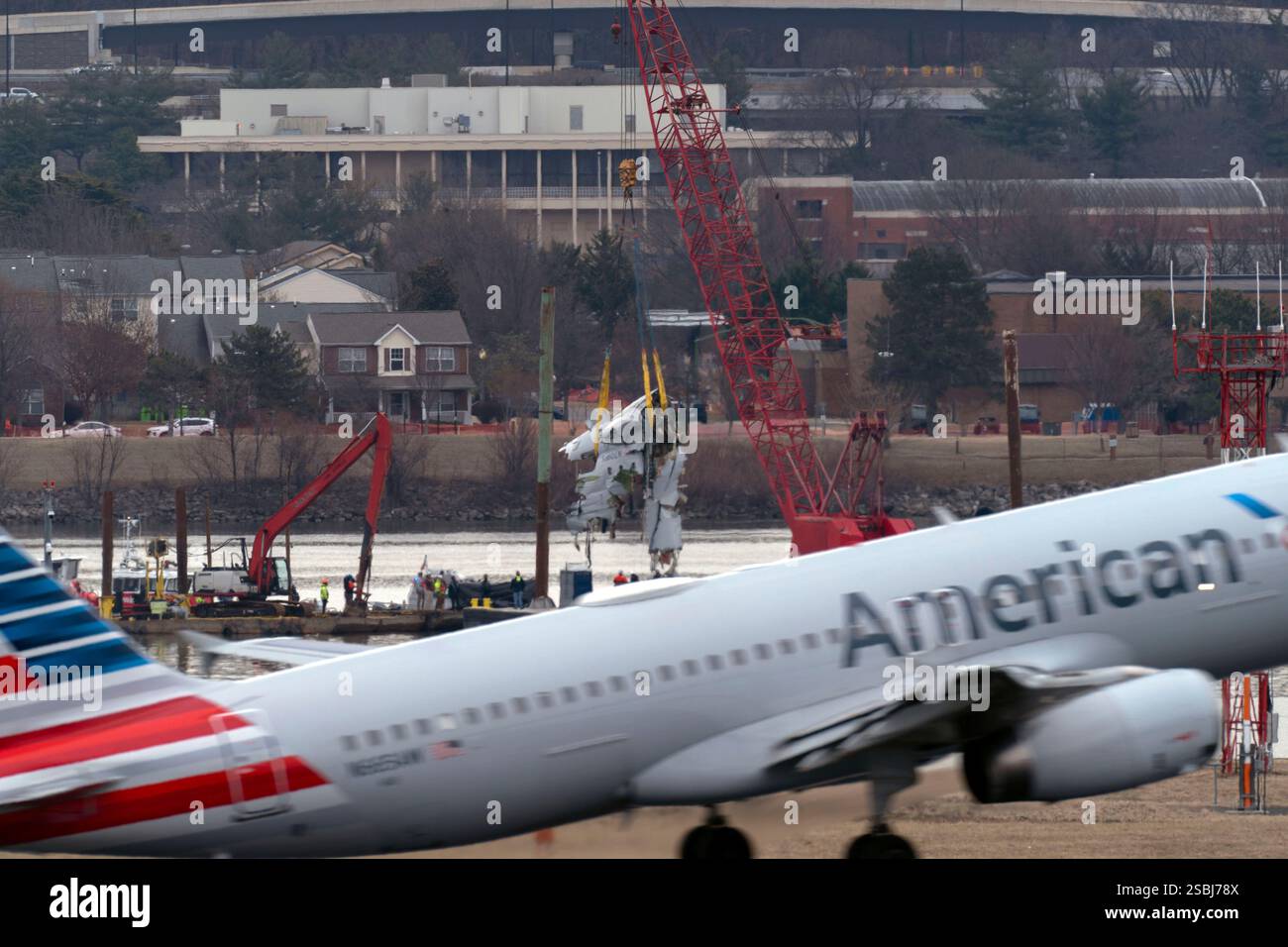 An American Airlines jet passes as rescue and salvage crews with cranes pull up the wreckage of ...