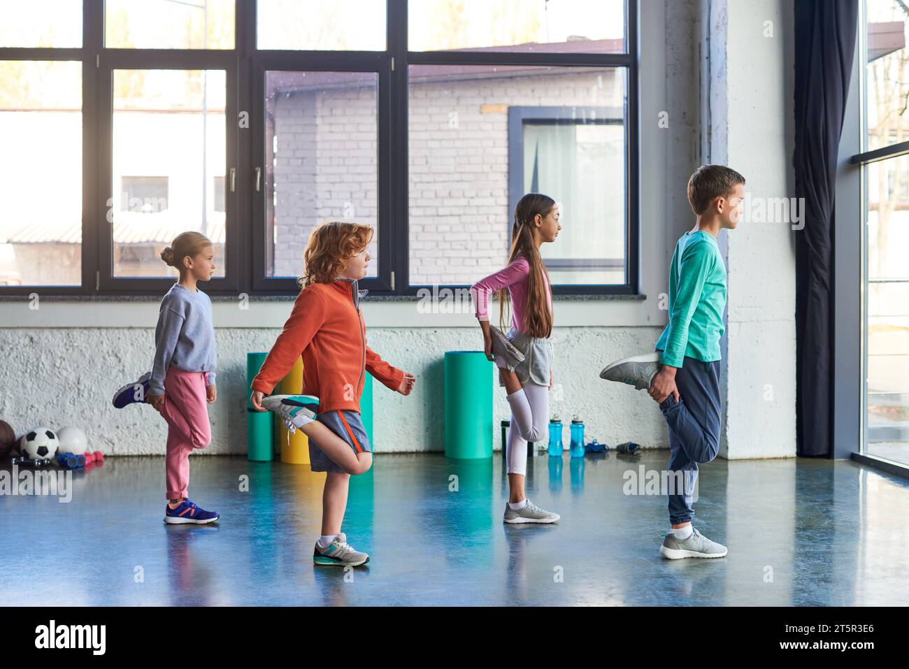 Vier vorpubertäre hübsche Kinder in Sportbekleidung, die ihre Beine im ...