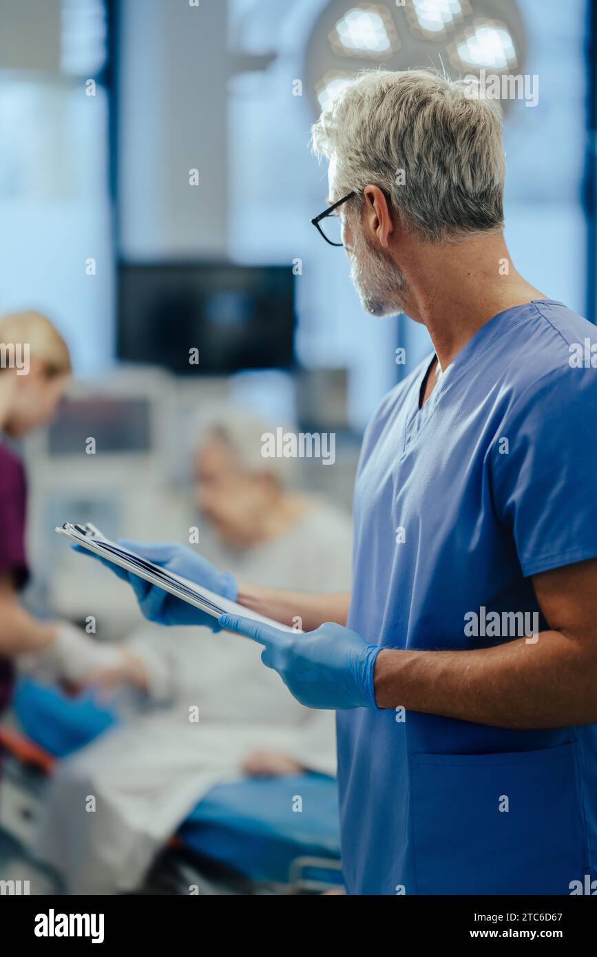 Reifer männlicher Arzt, der den Patienten im Krankenhausbett betrachtet ...