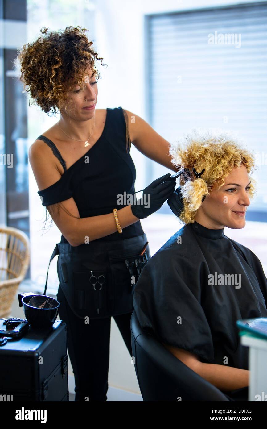 Professionelle Friseurin wendet sorgfältig Haarfarbe auf die lockigen ...