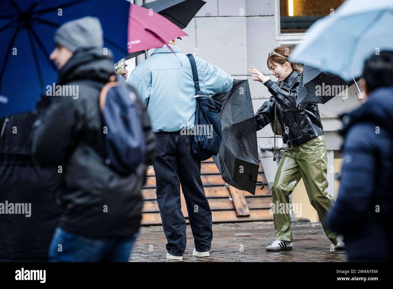 Touristen, die ihre Regenschirme halten, kämpfen mit dem Wind, während ...