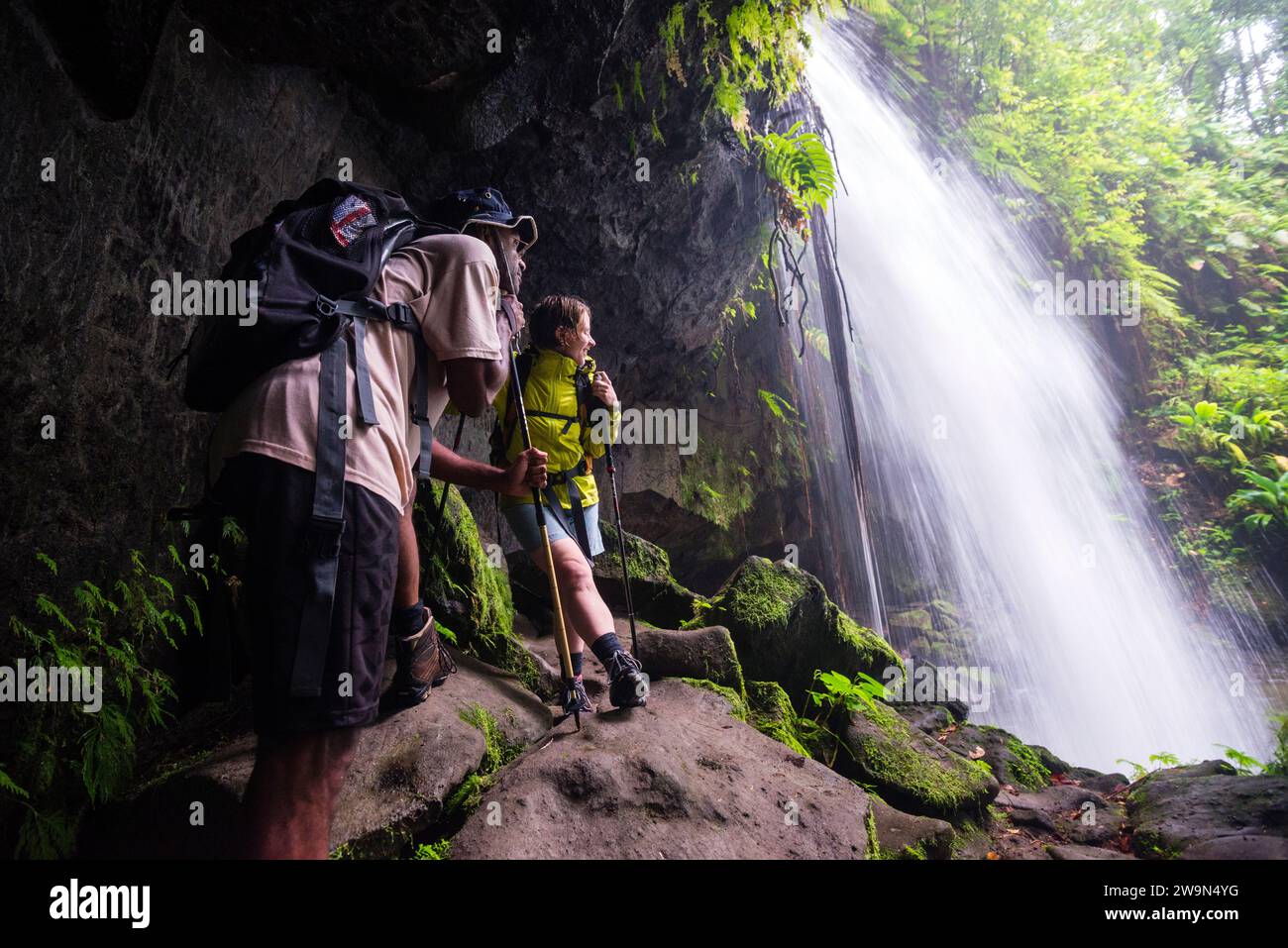 Eine Frau und ihr Reiseleiter stehen hinter einem Wasserfall, der in ...