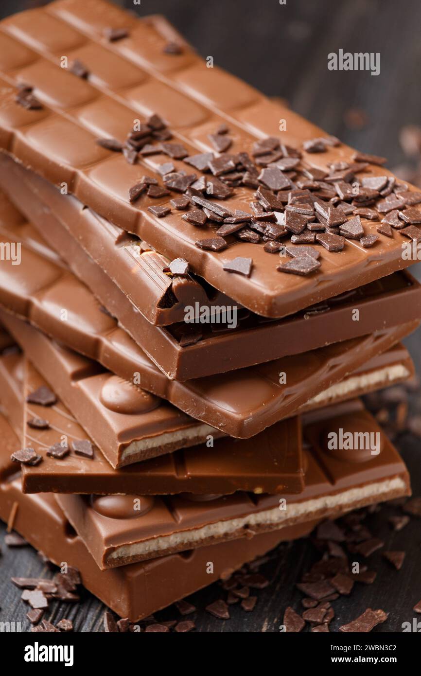 Ein Stapel ganze und gebrochene Schokoladentafeln und verstreute Schokoladentafeln auf hölzernem ...