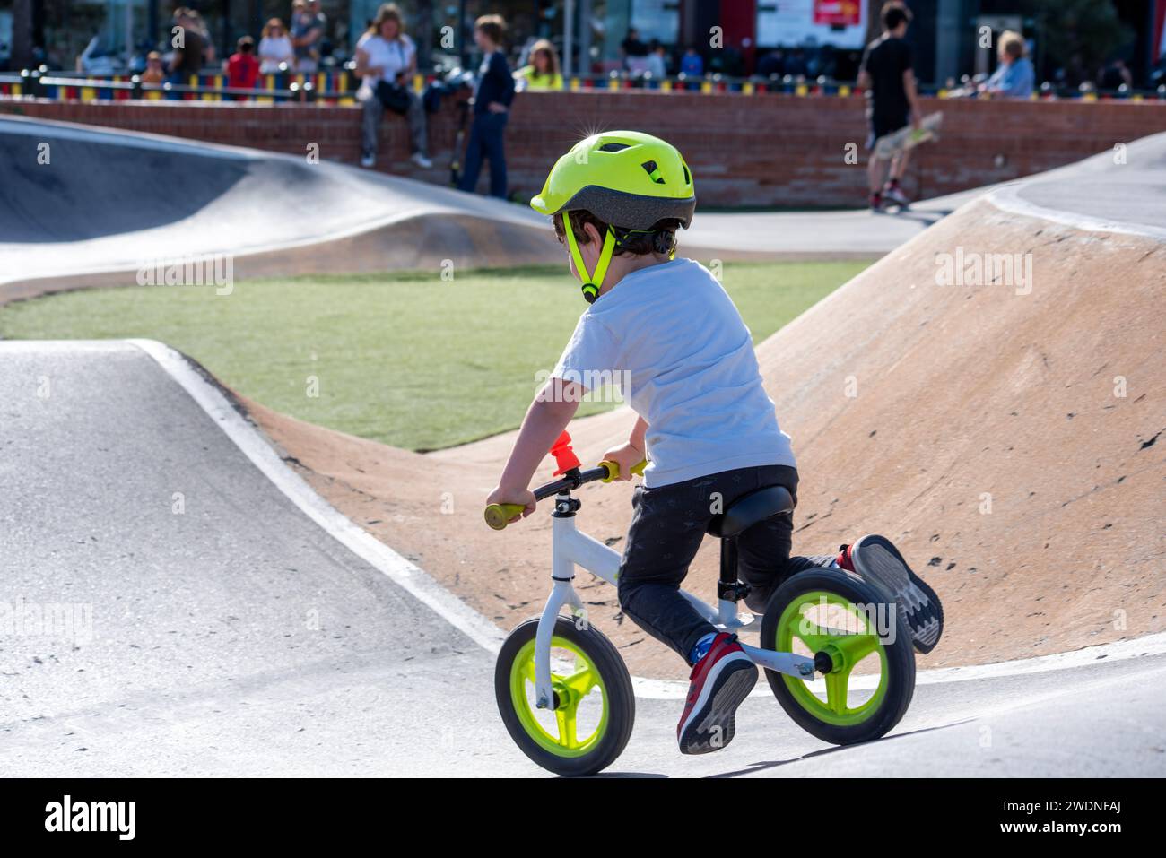 Lebhafte Pumptrack-Fahrt: Kind im Helm auf einem weißen und ...