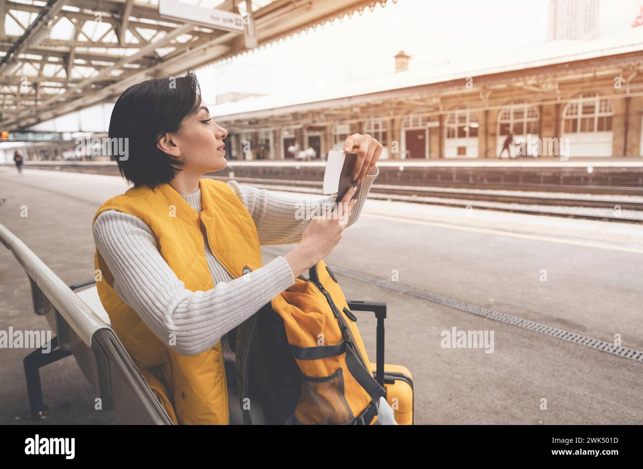 Junge Frau mit Pass und Fahrkarten, die am Bahnhof auf den Zug wartet und das Reisekonzept ...