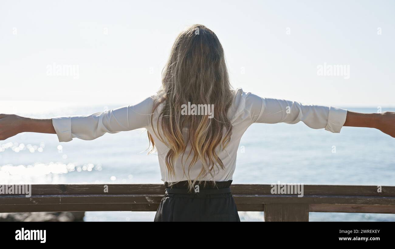 Die schöne junge blonde Frau steht lässig, die Arme offen, mit Blick ...