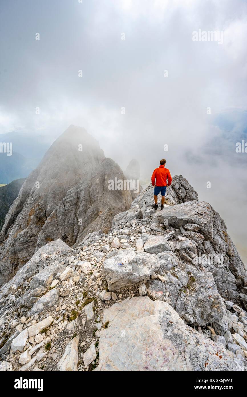 Bergsteiger auf einem felsigen schmalen Gipfelgrat, bewölkter ...