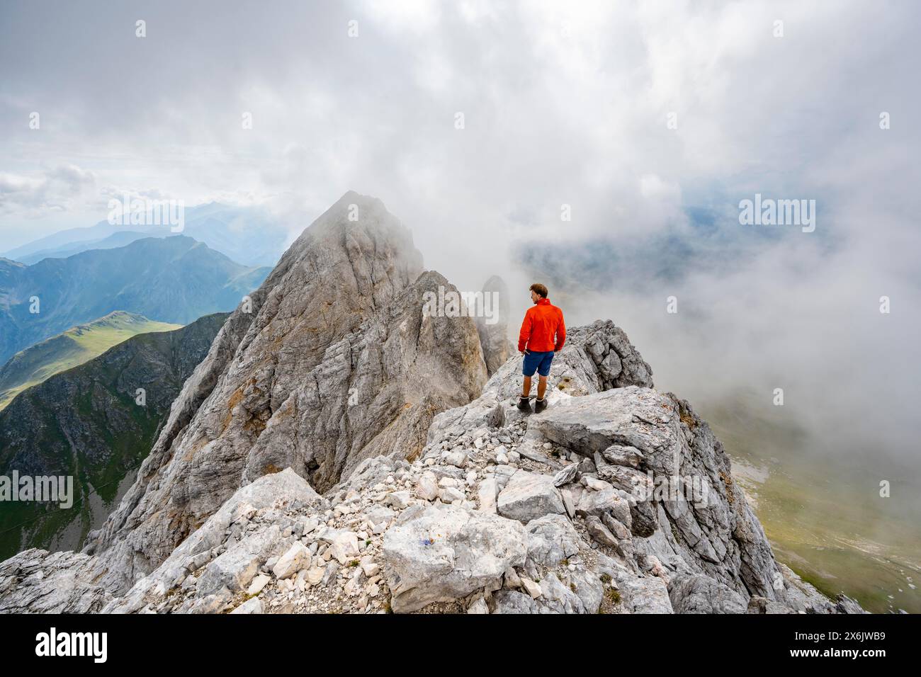 Bergsteiger auf einem felsigen schmalen Gipfelgrat, bewölkter ...