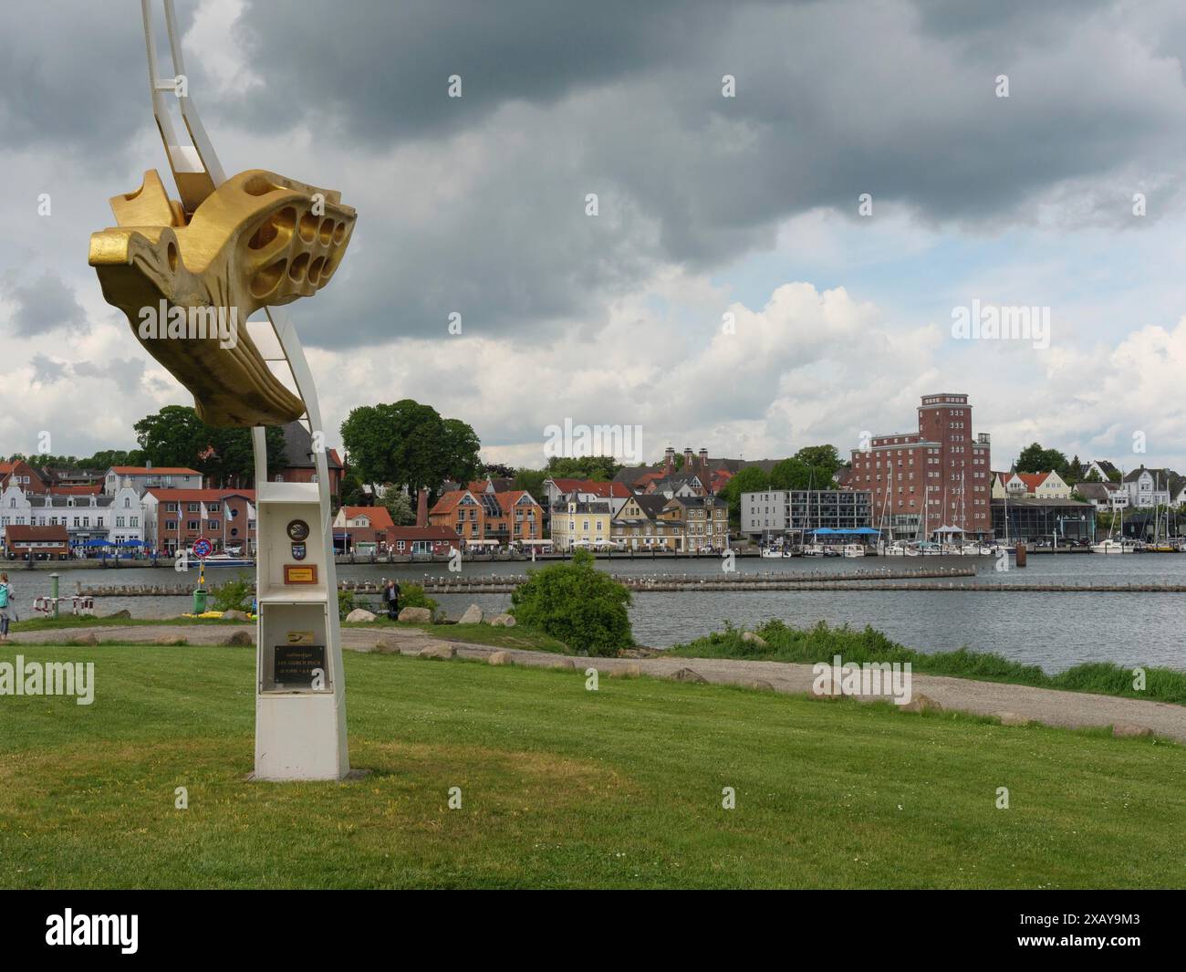 Eine goldene Skulptur erhebt sich vor einer malerischen Stadt am Wasser ...