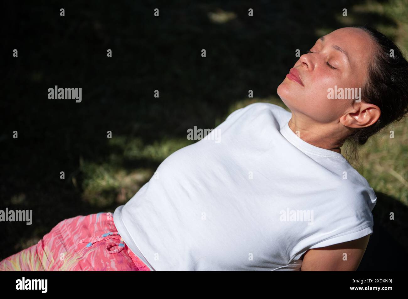 Eine Frau in einem weißen Hemd und einer bunten Hose, die einen friedlichen Moment in der Sonne ...