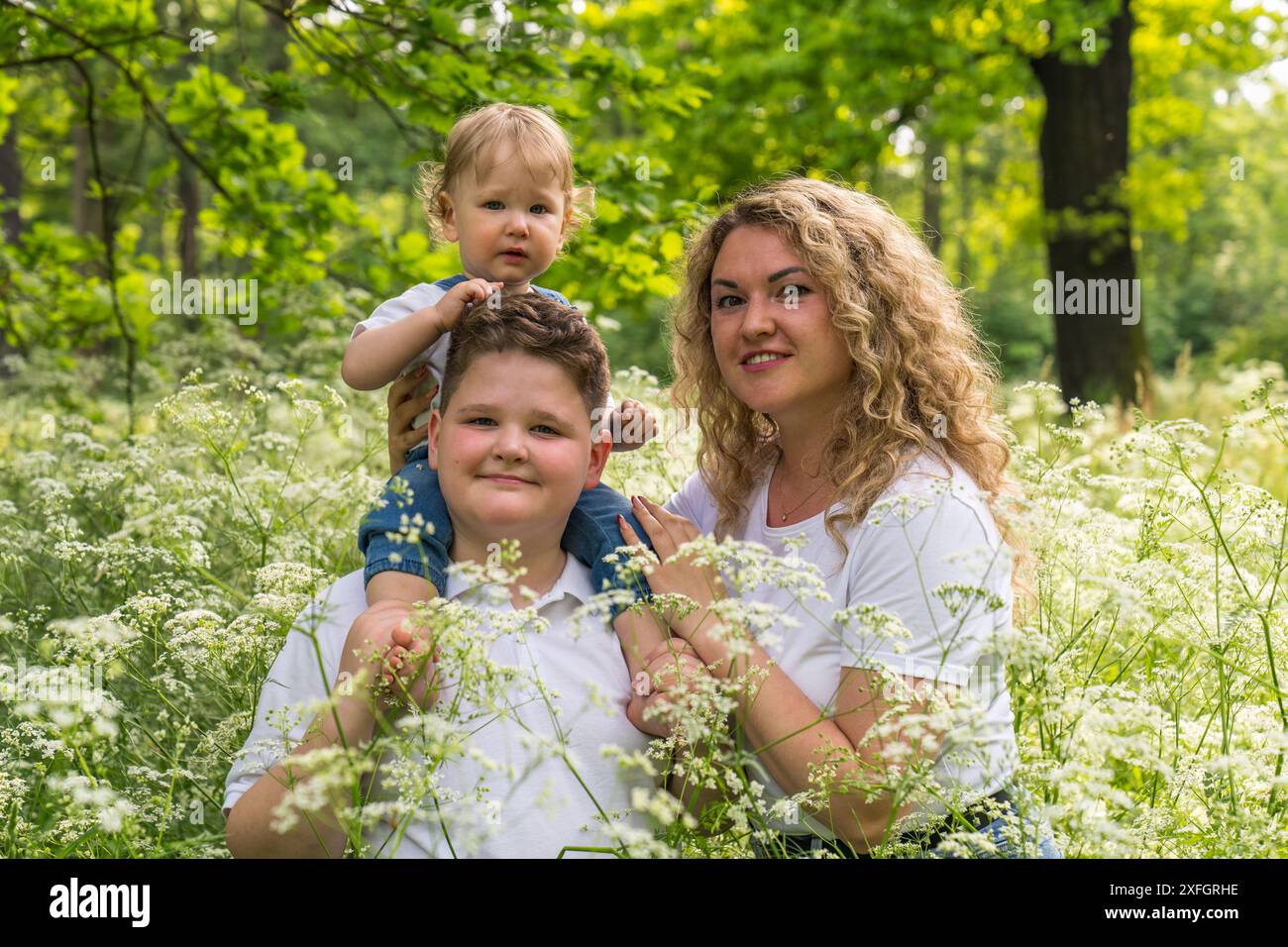 Mom mit zwei Söhnen im dicken Gras. Der ältere Bruder hält ein kleines ...