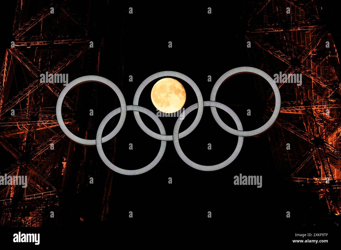 A full moon rises behind the Olympic rings hanging from the Eiffel ...