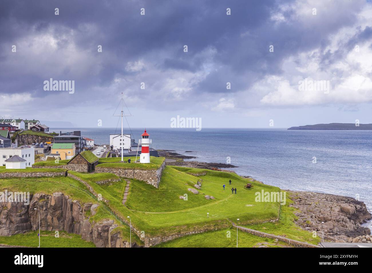 Ein kleiner rot-weißer Leuchtturm steht auf einem grünen Hügel bei ...