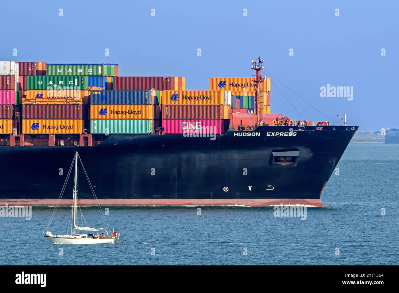 Segelboot fährt am Bug des Containerschiffs vorbei / Containerschiffschiff Hudson Express der ...