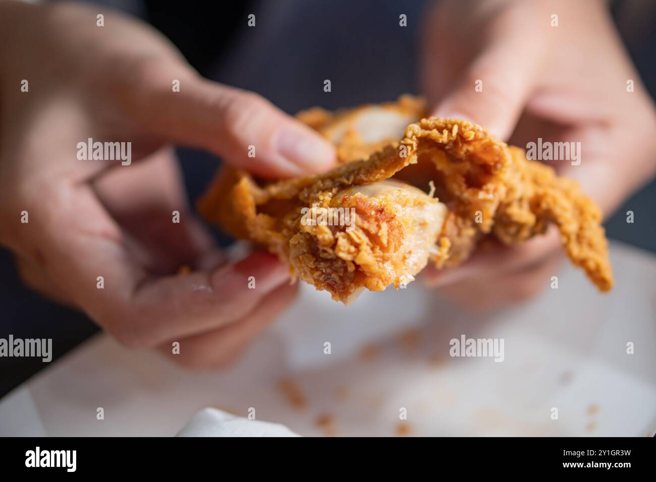 Eine Nahaufnahme der Hände, die ein Stück knuspriges gebratenes Huhn ...