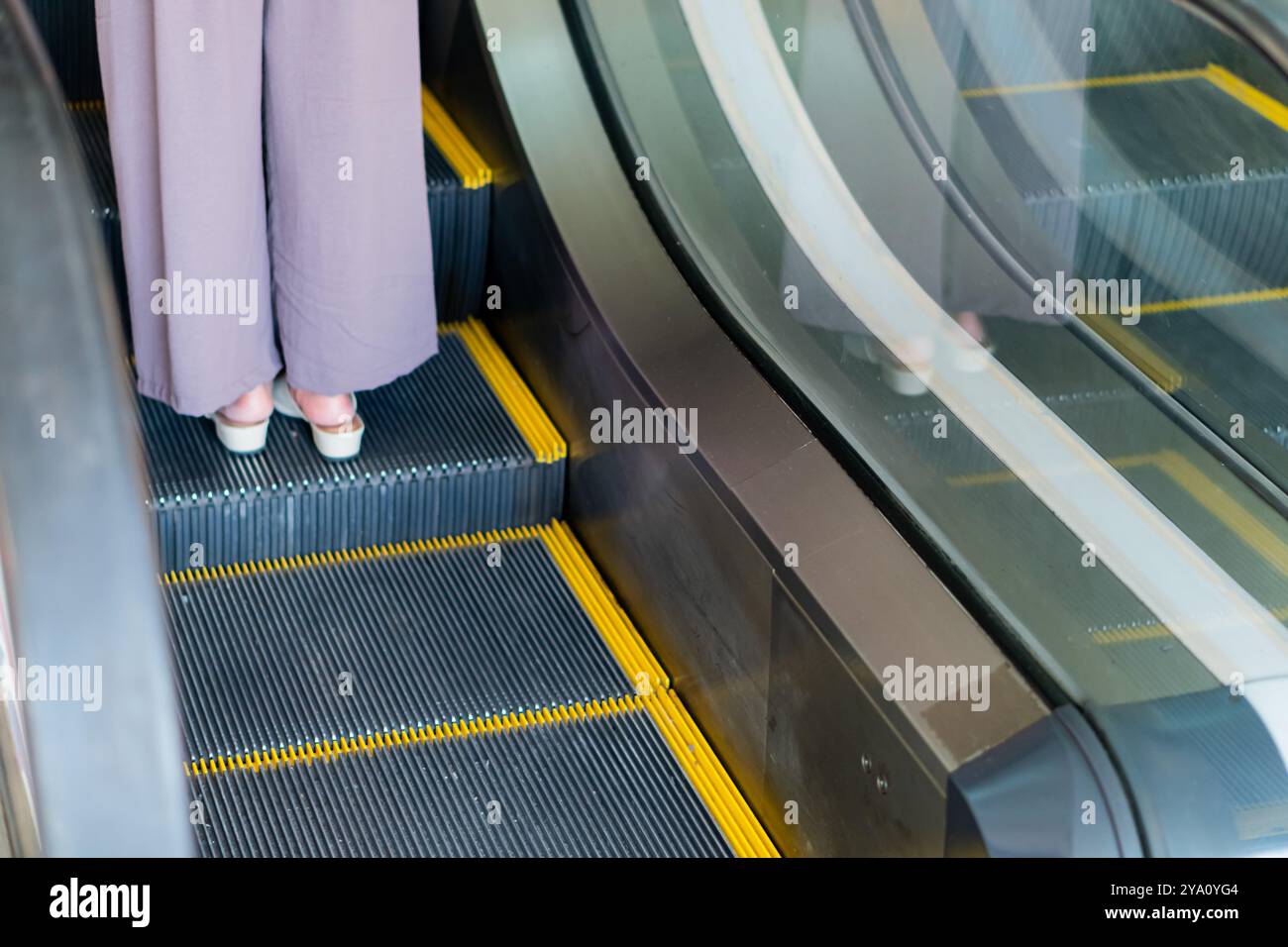 Nahaufnahme einer Person, die auf einer Rolltreppe steht und ihre Füße in stilvollen Schuhen ...