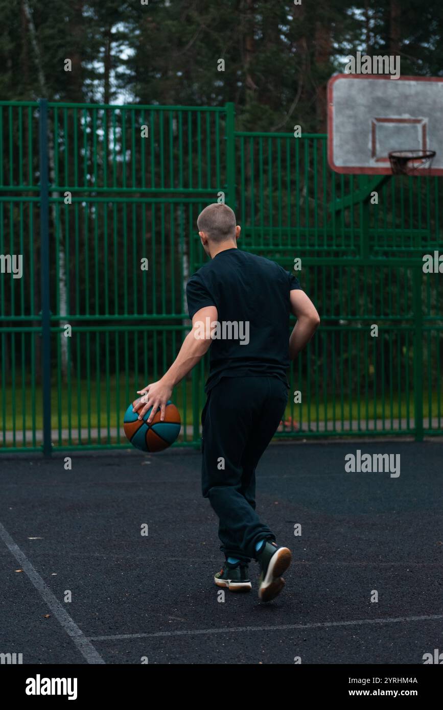 Ein junger Mann übt Basketball auf einem Freiluftplatz und dribbelt ...