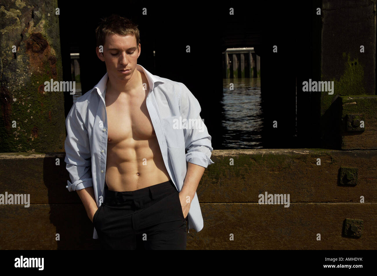 Jung, gesund, gut gebauter Mann sitzt auf dem Steg mit seinem Hemd ...