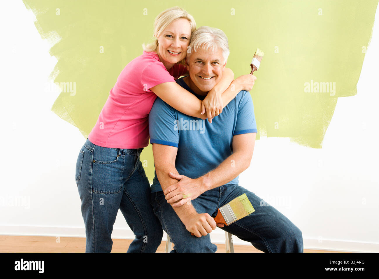 Porträt des Lächelns erwachsenes paar sitzen vor halb gemalt Wand mit ...