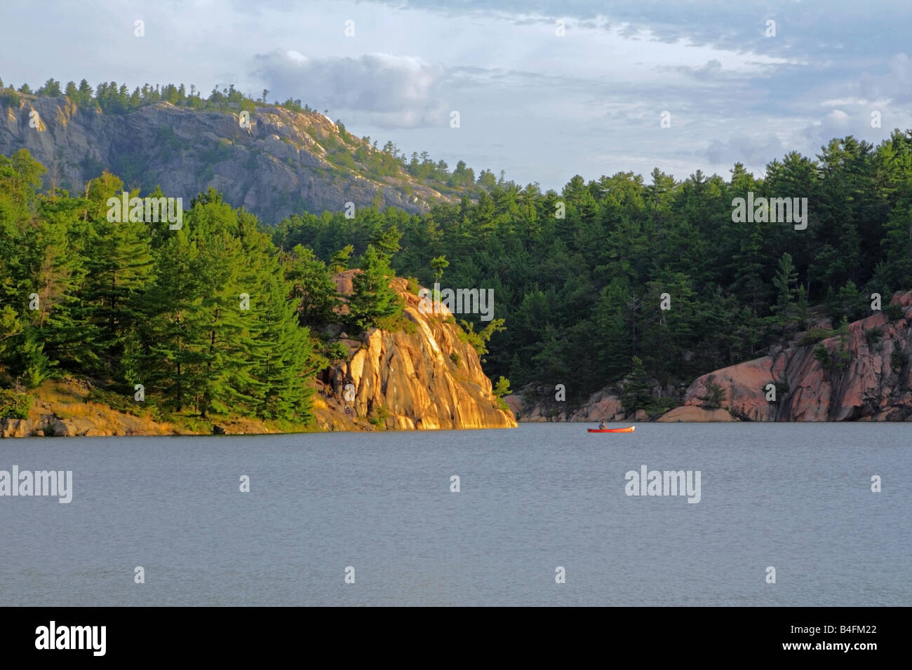 Morgenlicht auf rot und rosa Granitfelsen und Kanu in Lake George im ...