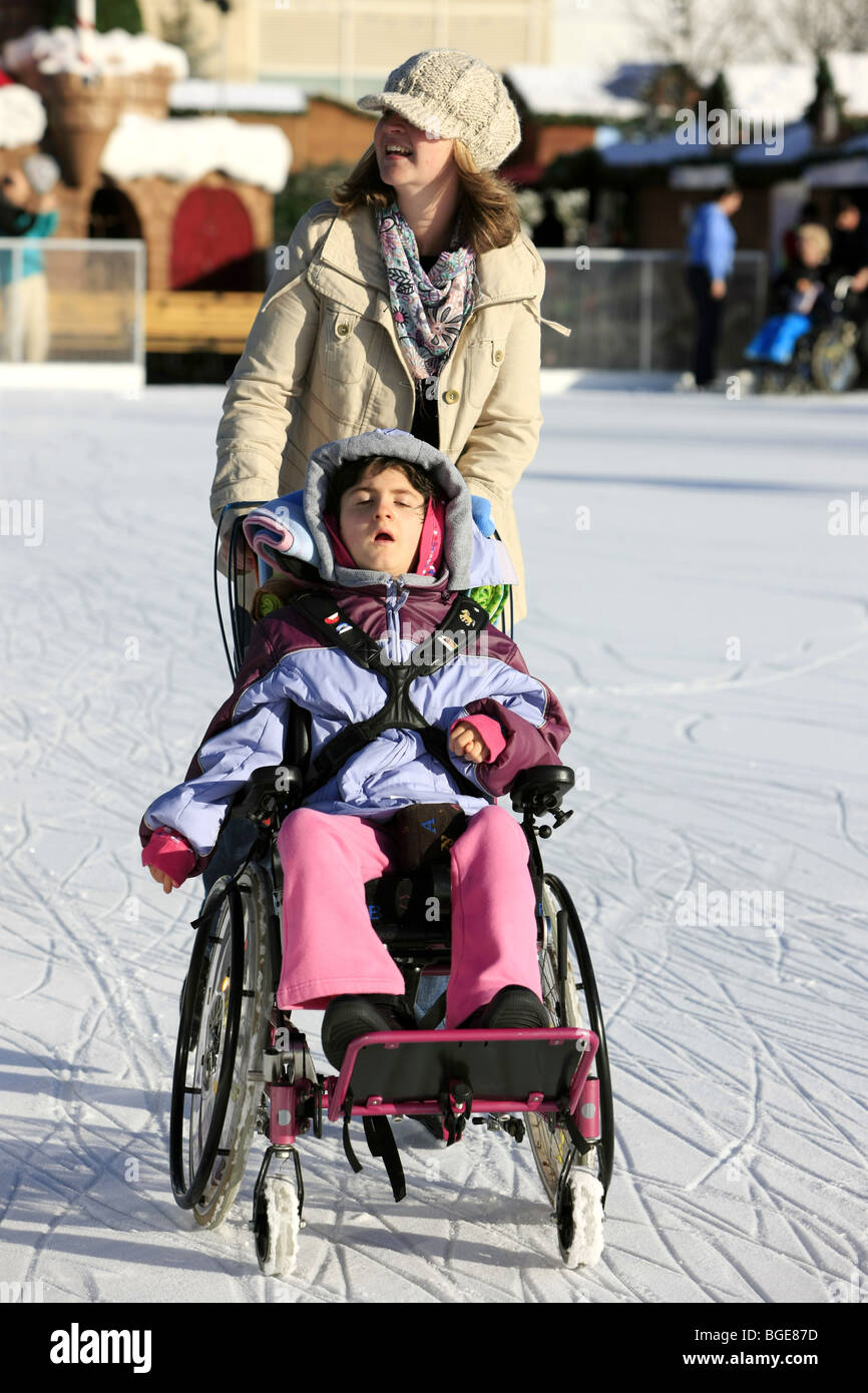 Behindertes Kind im Rollstuhl geschoben um eine Eisbahn durch eine ...