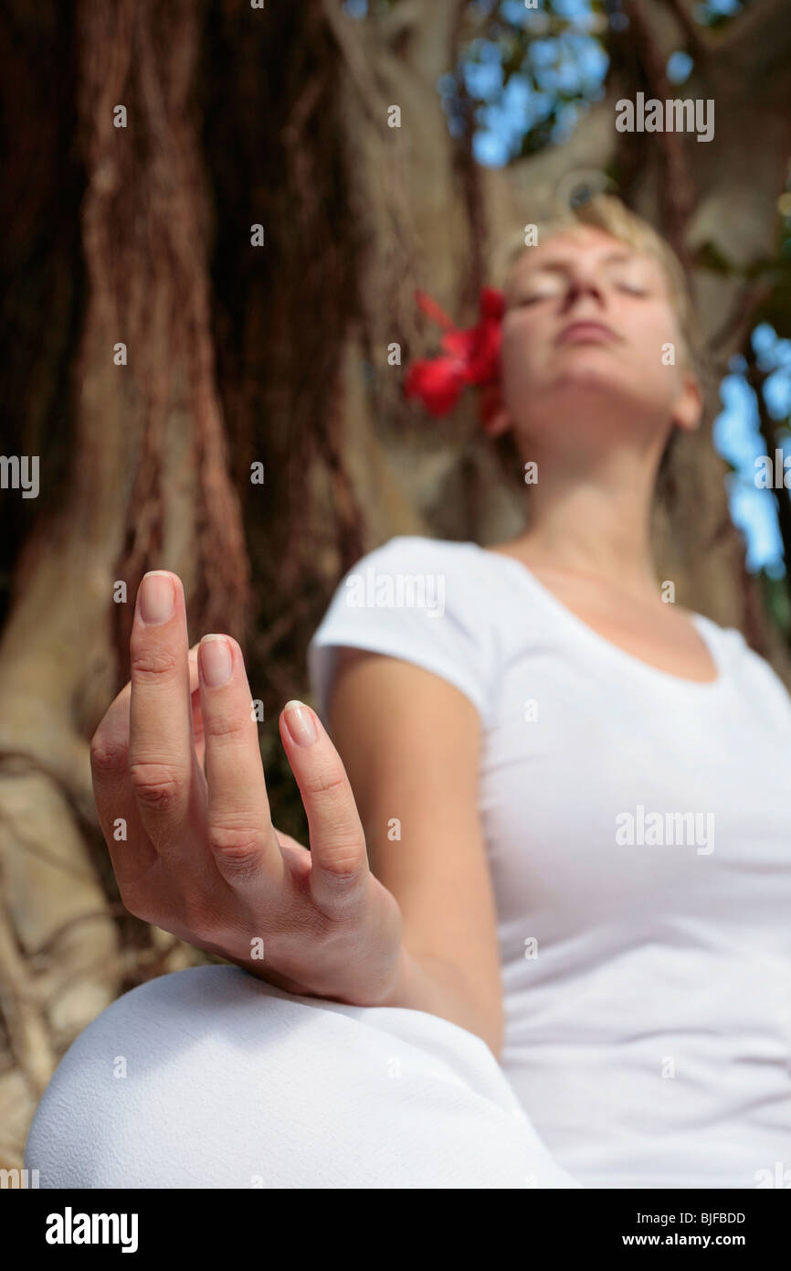 Frau in einem Yoga-Pose unter einem Bodhi-Baum mit einer Blume im Haar ...