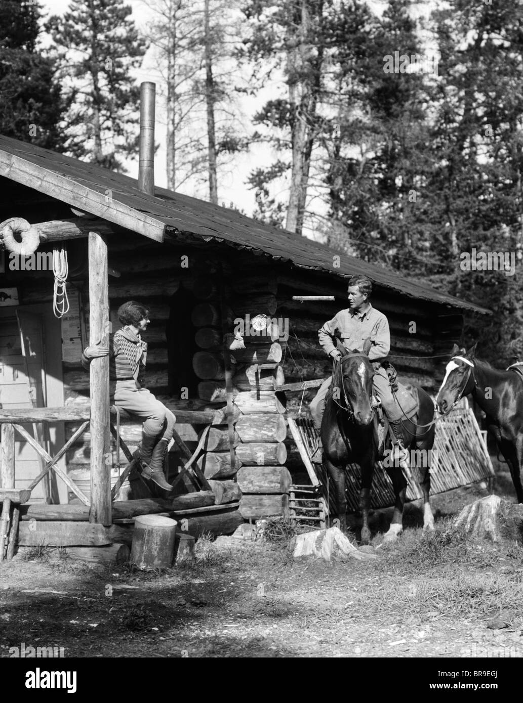 1920S 1930S PAAR VOR BLOCKHÜTTE FRAU SITZT AUF DER VERANDA GELÄNDER ...