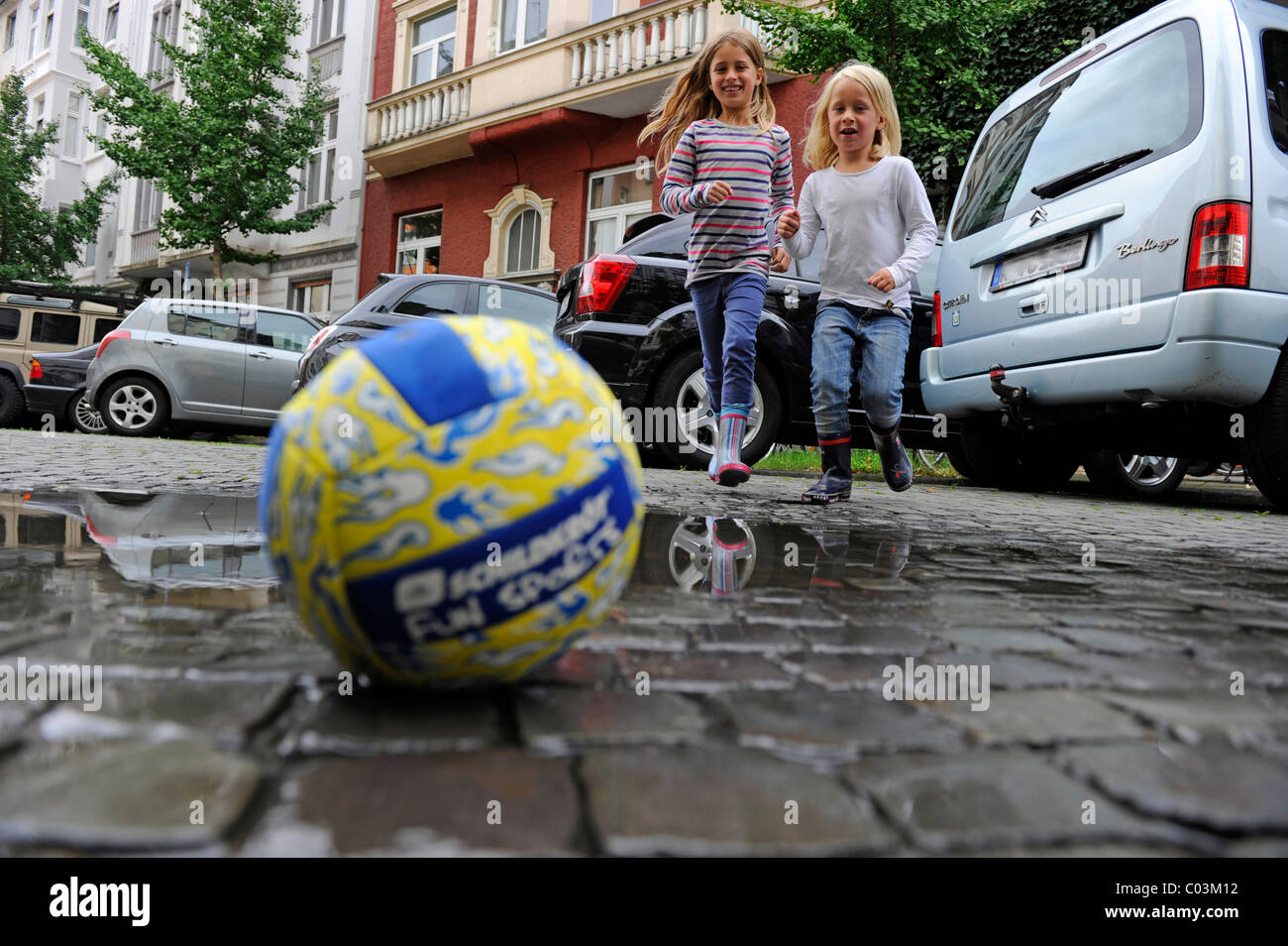 Zwei Mädchen laufen nach einem Ball auf einer Straße während des ...