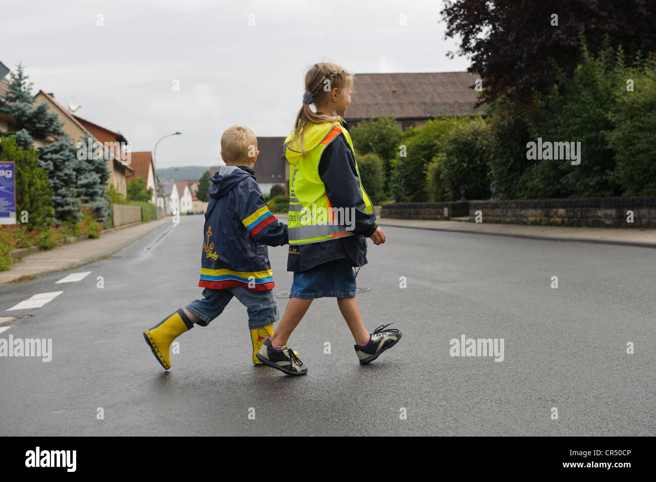 Zwei Kinder, 3 und 7 Jahren, überqueren der Straße im Regen, Assamstadt ... Zwei Kinder, 3 und 7 Jahren, überqueren der Straße im Regen, Assamstadt ...