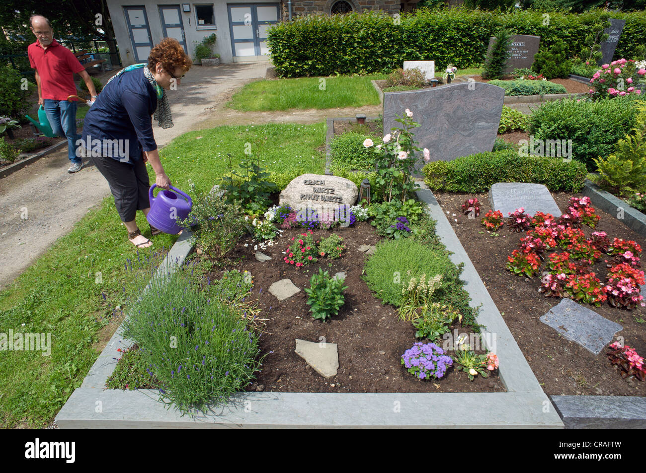 Frau auf einem Grab auf dem deutschen Friedhof Blumen gießen ...