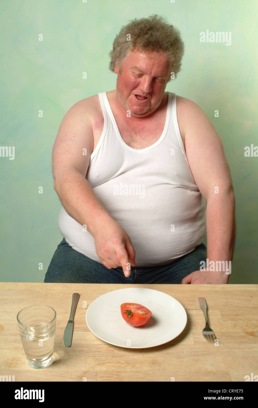 Fetter Mann im Unterhemd sitzt vor einem Teller mit einer halben Tomate ...