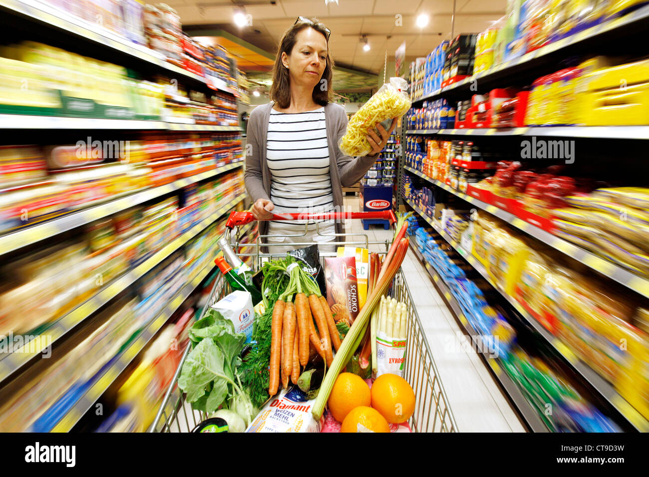 Grosser Supermarkt, Frau schiebt einen vollen Einkaufswagen entlang der ...